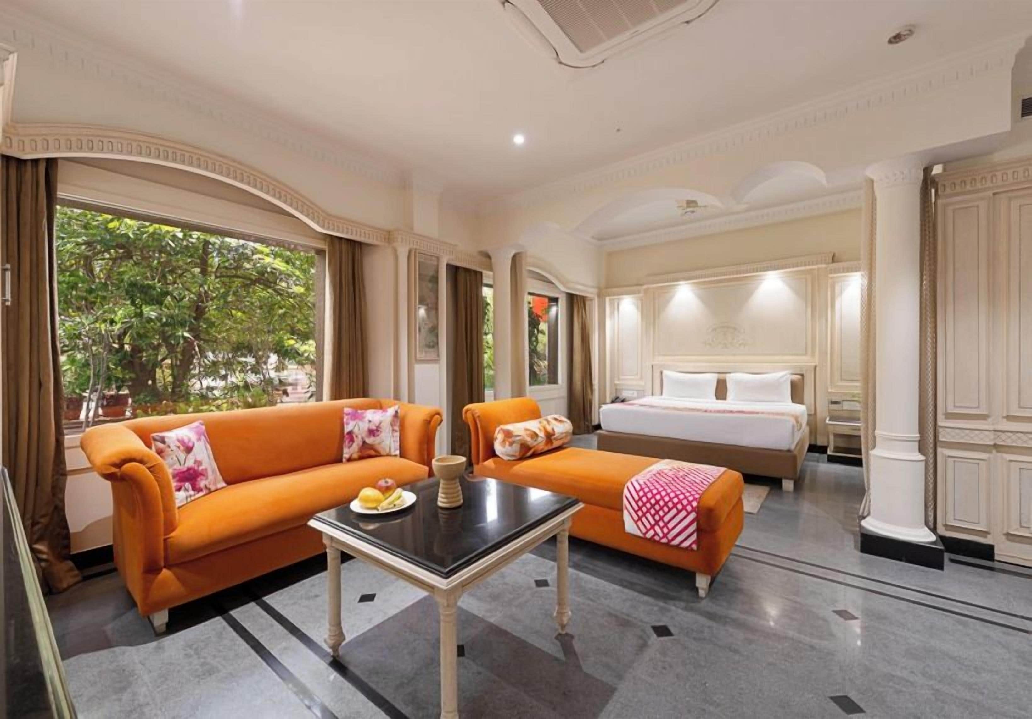 Quarto de hotel com sofá, cama, mesa e vista para o verde lá fora.