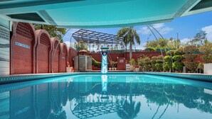 Piscina transparente com um toboágua central, rodeada por um muro de tijolos e palmeiras.