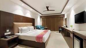 Quarto de hotel com cama, escrivaninha, cadeira, televisão e ventoinha no teto.