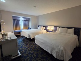 Quarto de hotel com duas camas, uma mesa de trabalho e uma janela com cortinas.