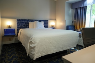 Quarto de hotel com uma cama grande, duas luminárias de cabeceira, uma escrivaninha e uma cadeira.
