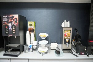 A coffee station with a Nescafé machine, disposable cups, condiment dispensers, and a waffle maker.