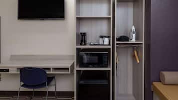 Quarto de hotel com televisão de tela plana na parede, micro-ondas, cafeteira e tábua de passar.
