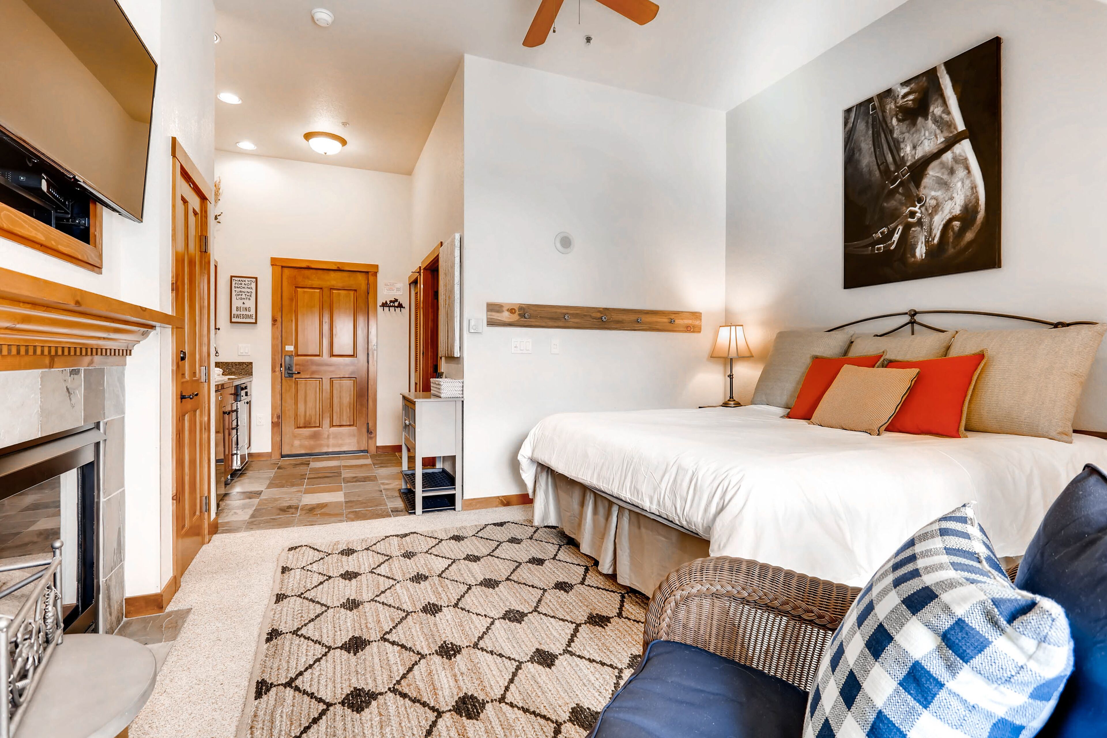 Quarto com cama, lareira, cozinha ao fundo e corredor que dá para outro espaço.