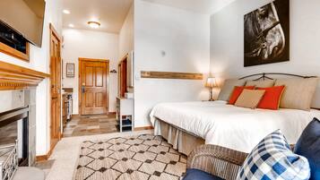 Quarto com cama, lareira, cozinha ao fundo e corredor que dá para outro espaço.