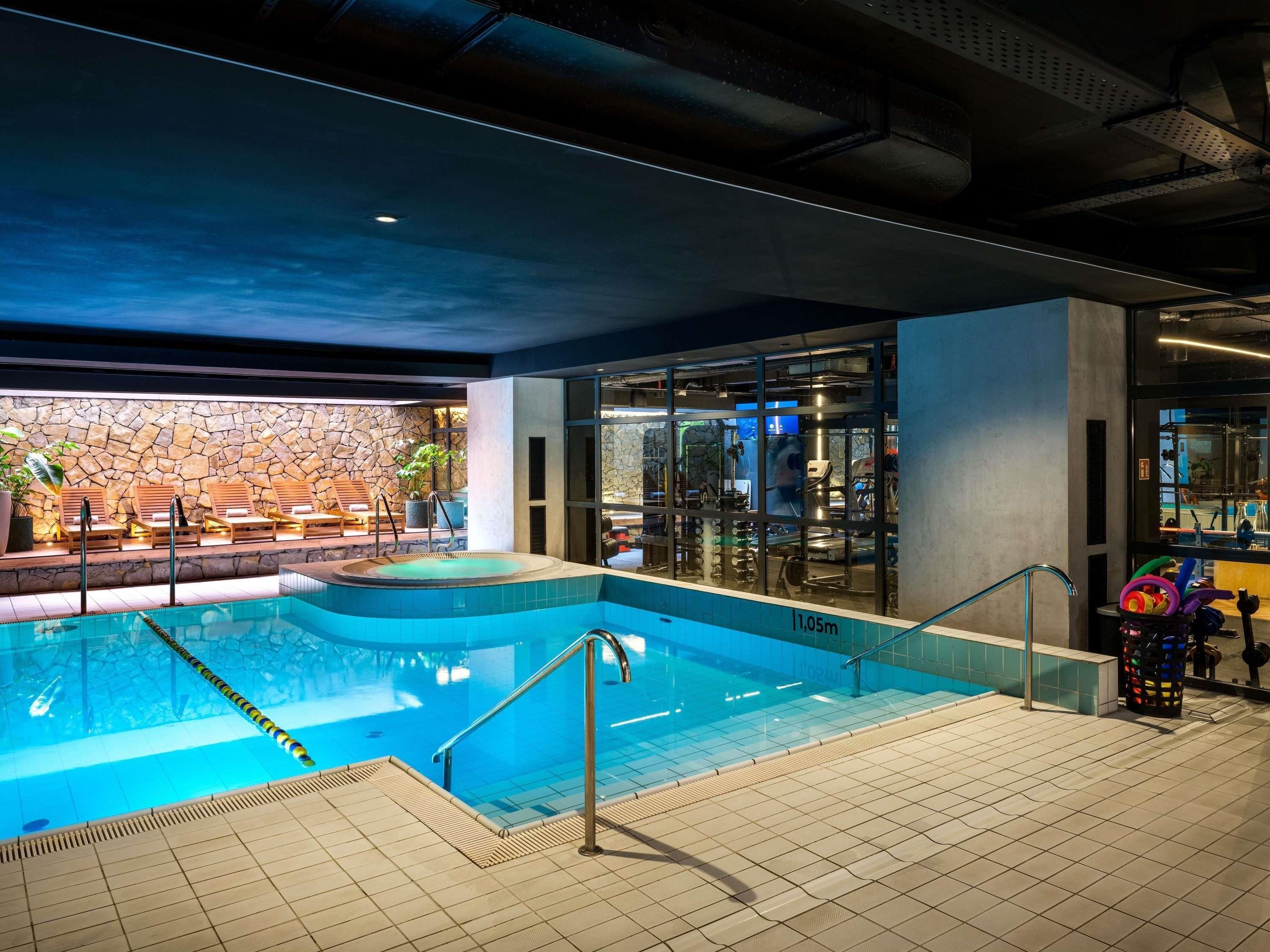 Piscina interior com parede de pedra, cadeiras de descanso e equipamentos de ginástica.