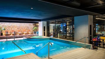 Piscina interior com parede de pedra, cadeiras de descanso e equipamentos de ginástica.