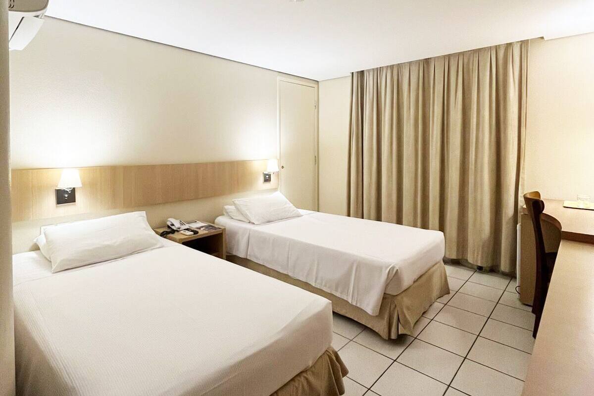Quarto de hotel com duas camas de solteiro, uma escrivaninha e uma cadeira.