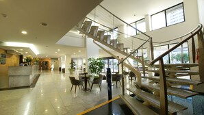 Um hall amplo com escadaria moderna, balcão de recepção e diversas áreas de estar.