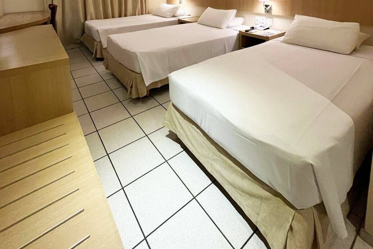 Quarto de hotel com três camas de solteiro, um sofá, uma escrivaninha e uma obra de arte na parede.