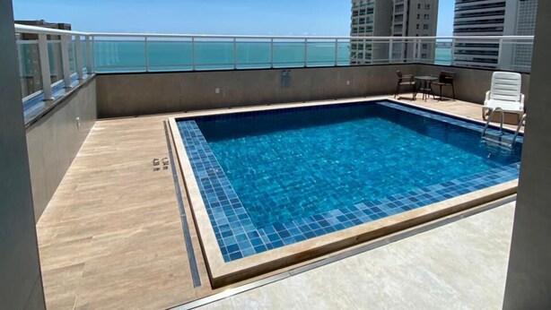 Piscina no terraço com vista clara para o oceano e edifícios ao fundo.