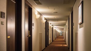 Corredor de hotel com portas em ambos os lados, piso coberto de carpete e iluminação embutida.