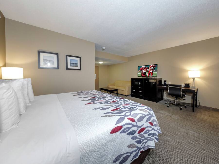 Quarto de hotel com uma cama grande, uma escrivaninha com cadeira, televisão e duas molduras na parede.