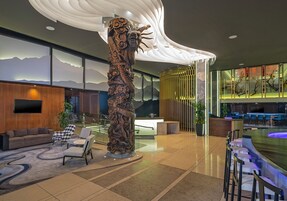 Um lobby moderno com uma grande escultura de dragão, balcão de recepção, área de estar e um bar.