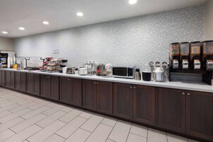 Uma cozinha moderna com um balcão comprido, equipada com cafeteiras, micro-ondas e um espaço para café.