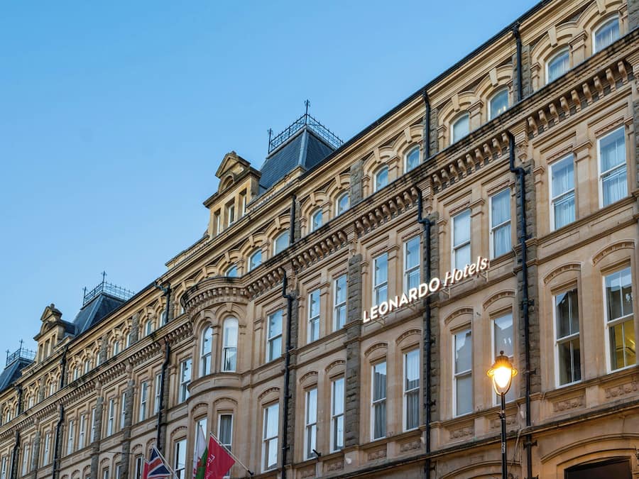 Um edifício histórico com a placa 'LEONARDO Hotels', apresentando arquitetura clássica com várias janelas e uma entrada imponente.