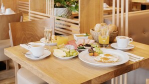 Uma mesa de madeira com café da manhã, pratos de comida, copos de suco e uma xícara de café.