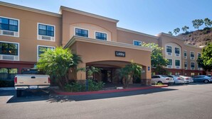 Um hotel com placa indicando 'Lobby', vários espaços de estacionamento e um edifício de fachada bege.