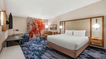 Quarto de hotel com uma cama grande, uma escrivaninha, uma cadeira, uma mesinha e um sofá.