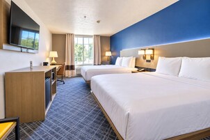 Quarto de hotel com duas camas, uma escrivaninha, uma televisão e uma janela com cortinas.