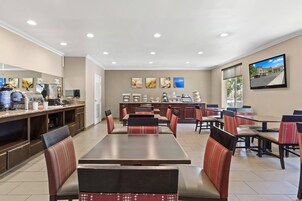 Uma área de refeições de hotel, com várias mesas e cabines, uma cozinha e uma televisão grande.