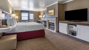 Quarto de hotel com uma cama grande, televisão de tela plana, lareira, escrivaninha com luminária e janela.