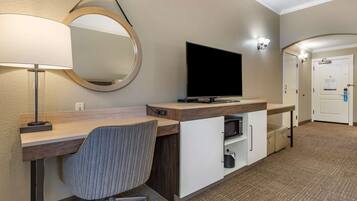 Quarto de hotel com escrivaninha, cadeira, televisão e armários.