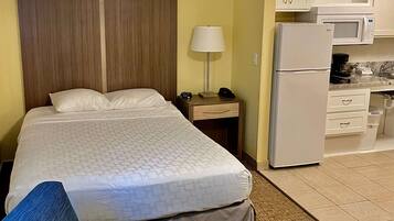 Quarto de hotel com cama, mesa de cabeceira, abajur, frigorífico e kitchenette.
