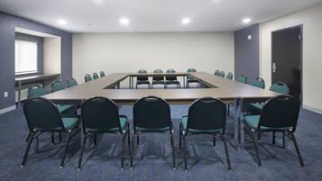 Sala de conferências com uma mesa longa e cadeiras, piso com carpete e tela de projetor.
