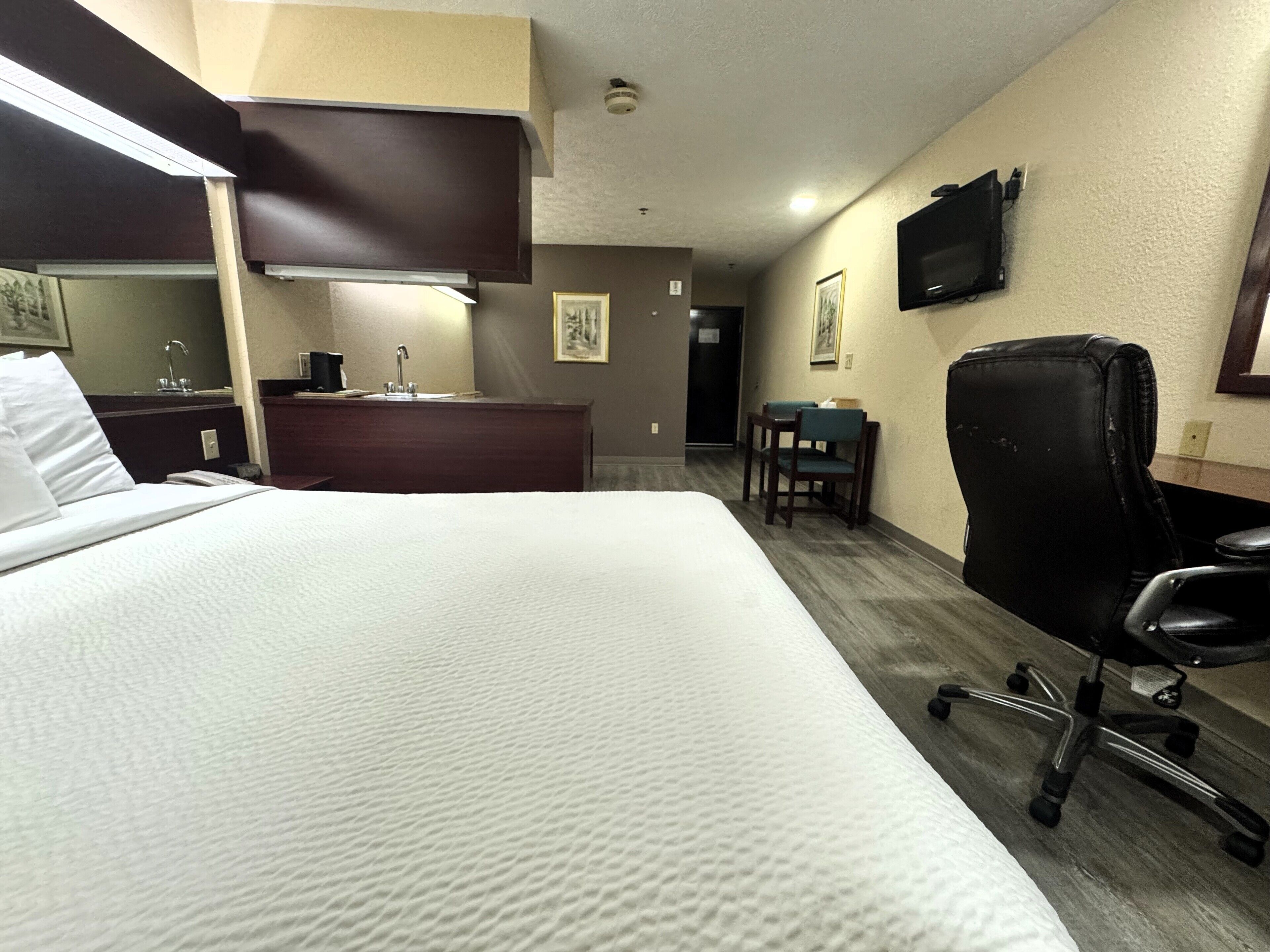Quarto de hotel com uma cama grande, uma secretária com cadeira, televisão na parede e casa de banho com lavatório e espelho.