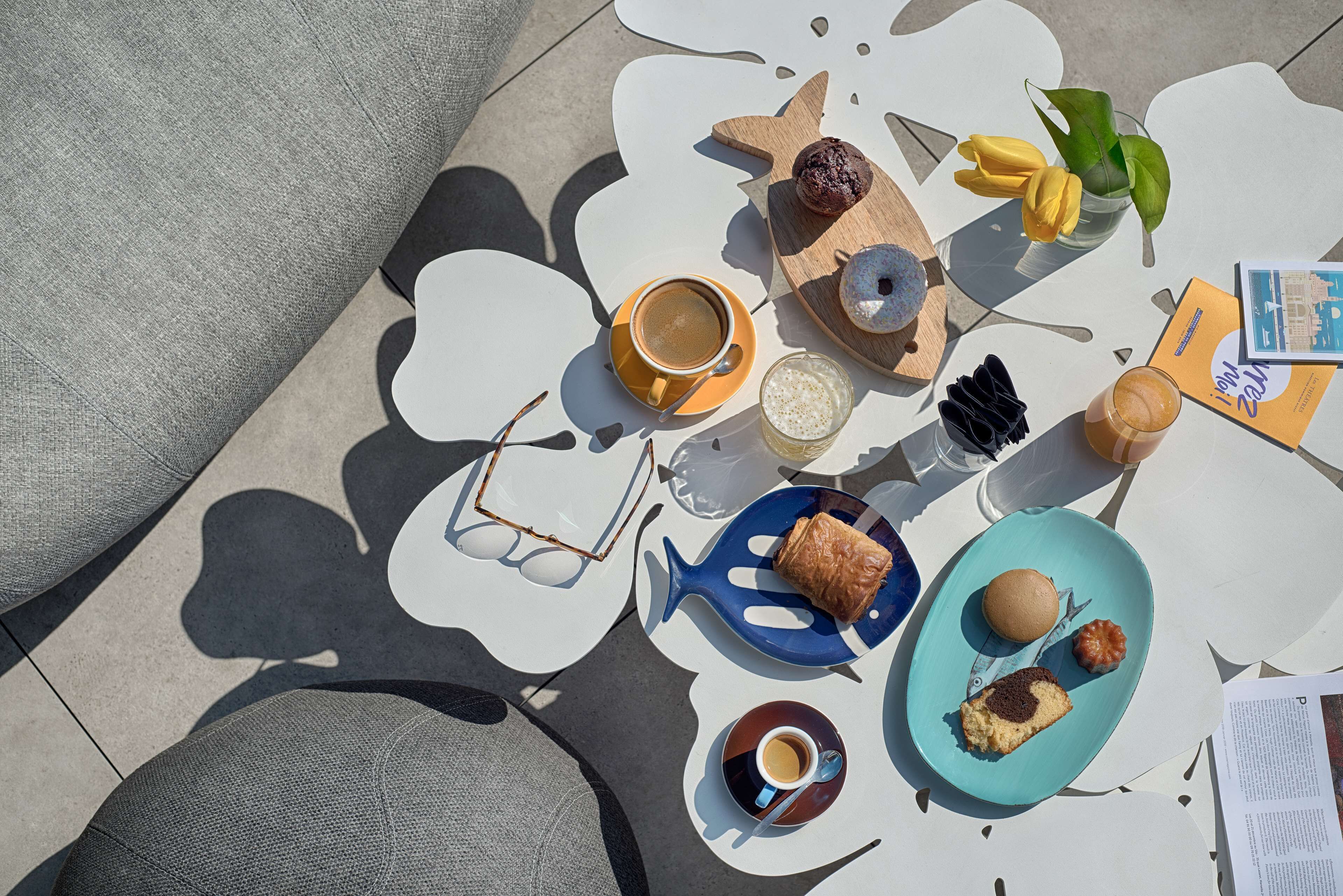 Uma mesa com diversos alimentos e bebidas, incluindo doces, uma xícara de café e um copo de suco.
