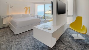Quarto de hotel moderno com uma cama, uma mesa de trabalho, uma televisão e vista para o mar.