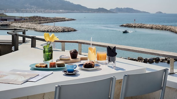Uma mesa com itens de café da manhã, um copo de líquido verde e uma flor amarela.