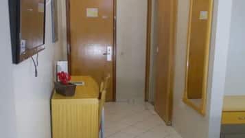 Quarto de hotel com uma cama, uma escrivaninha com cadeira, um espelho e uma porta.