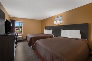 Quarto de hotel com duas camas, uma escrivaninha com televisão e janela com vista para um parque de estacionamento.