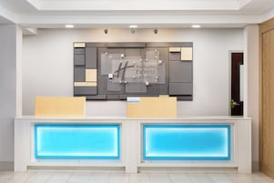 Bancada de recepção com design moderno, com uma grande placa fixada na parede e dois painéis azuis iluminados abaixo.