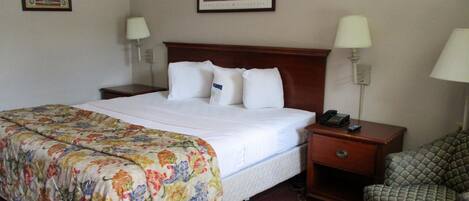 Quarto de hotel com uma cama grande, duas mesas de cabeceira, uma cadeira e duas luminárias fixadas na parede.