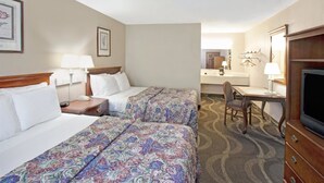 Quarto de hotel com duas camas, uma escrivaninha, uma cadeira, televisão e banheiro ao fundo.
