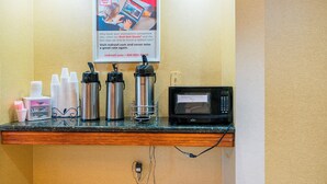 Uma área de recepção de hotel com um cartaz divulgando Red Roof Inn, um espaço para café com copos descartáveis, micro-ondas e chaleira.