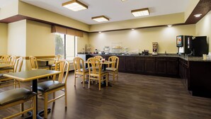 Restaurante com cadeiras e mesas de madeira, área de cozinha e máquina de café.