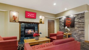 Um saguão de hotel com lareira, móveis estofados vermelhos, placa da Red Roof Inn e um aviso de 'Wi-Fi Grátis em Todos os Quartos'.