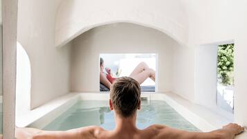 Um homem relaxa em uma piscina infinita branca, com vista para uma mulher de maiô vermelho.