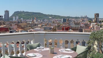 Terraço no telhado com uma mesa posta para refeições, com vista para um horizonte urbano com edifícios e uma colina.