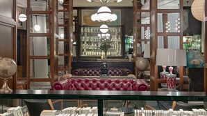 Uma biblioteca com estantes, poltronas de couro, um globo e um lustre.