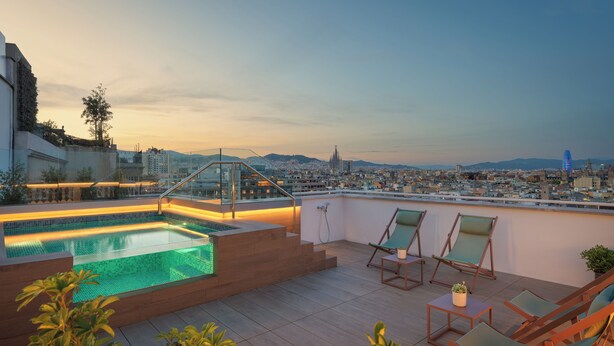 Terraço no telhado com piscina, espreguiçadeiras e vista para a cidade.