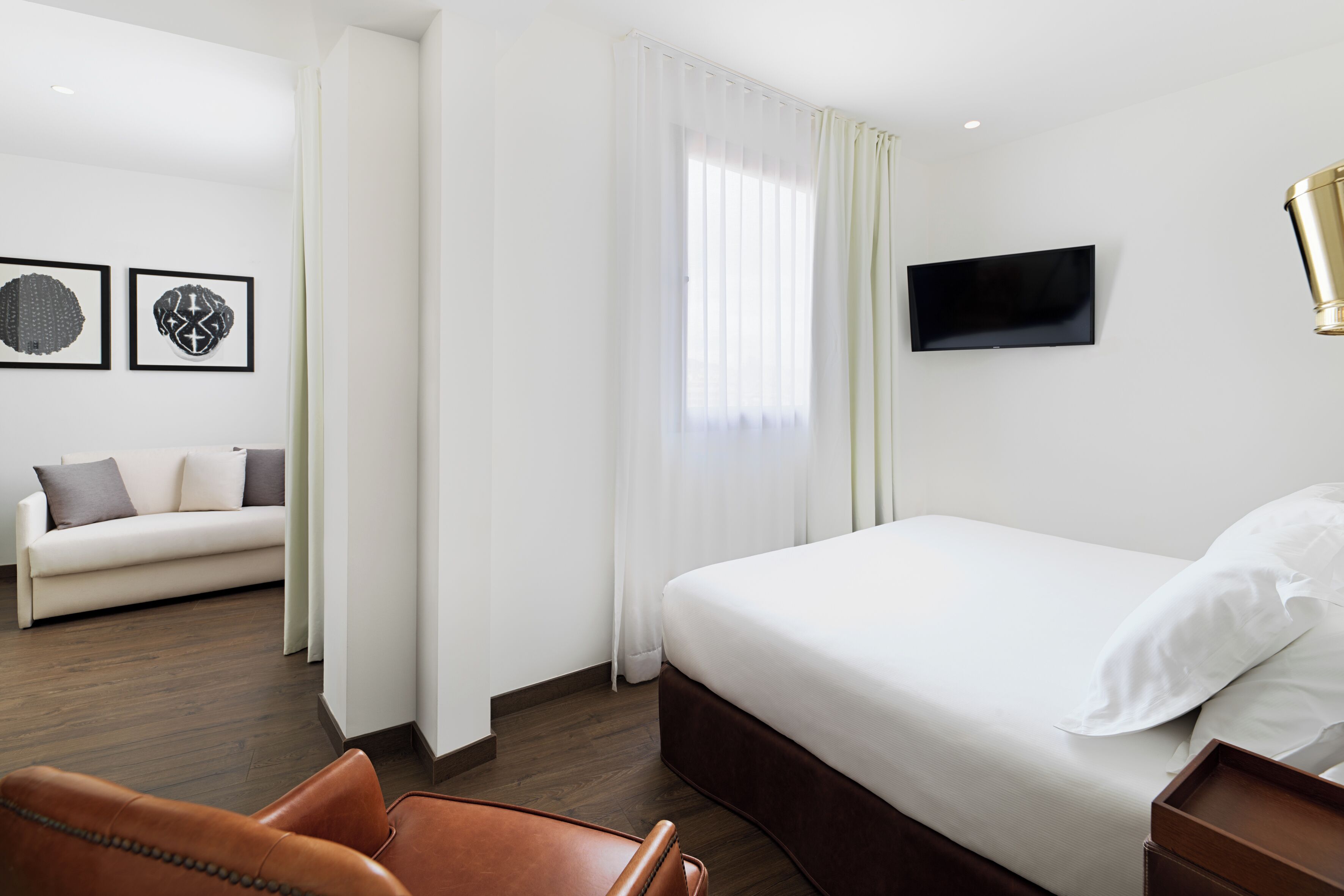 Quarto de hotel com cama, sofá, televisão e obras de arte na parede.