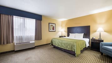 Quarto de hotel com cama, duas mesas de cabeceira com luminárias, uma janela com cortinas e ar condicionado fixado na parede.