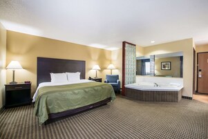 Quarto de hotel com uma cama grande, duas luminárias de cabeceira, uma cadeira, uma banheira e um espelho.