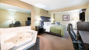 Quarto de hotel com uma banheira grande, uma cama com manta verde, duas mesas de cabeceira com abajures, uma escrivaninha e uma cadeira.