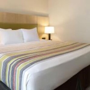 Quarto de hotel com cama, travesseiros, mesa de cabeceira e abajur.